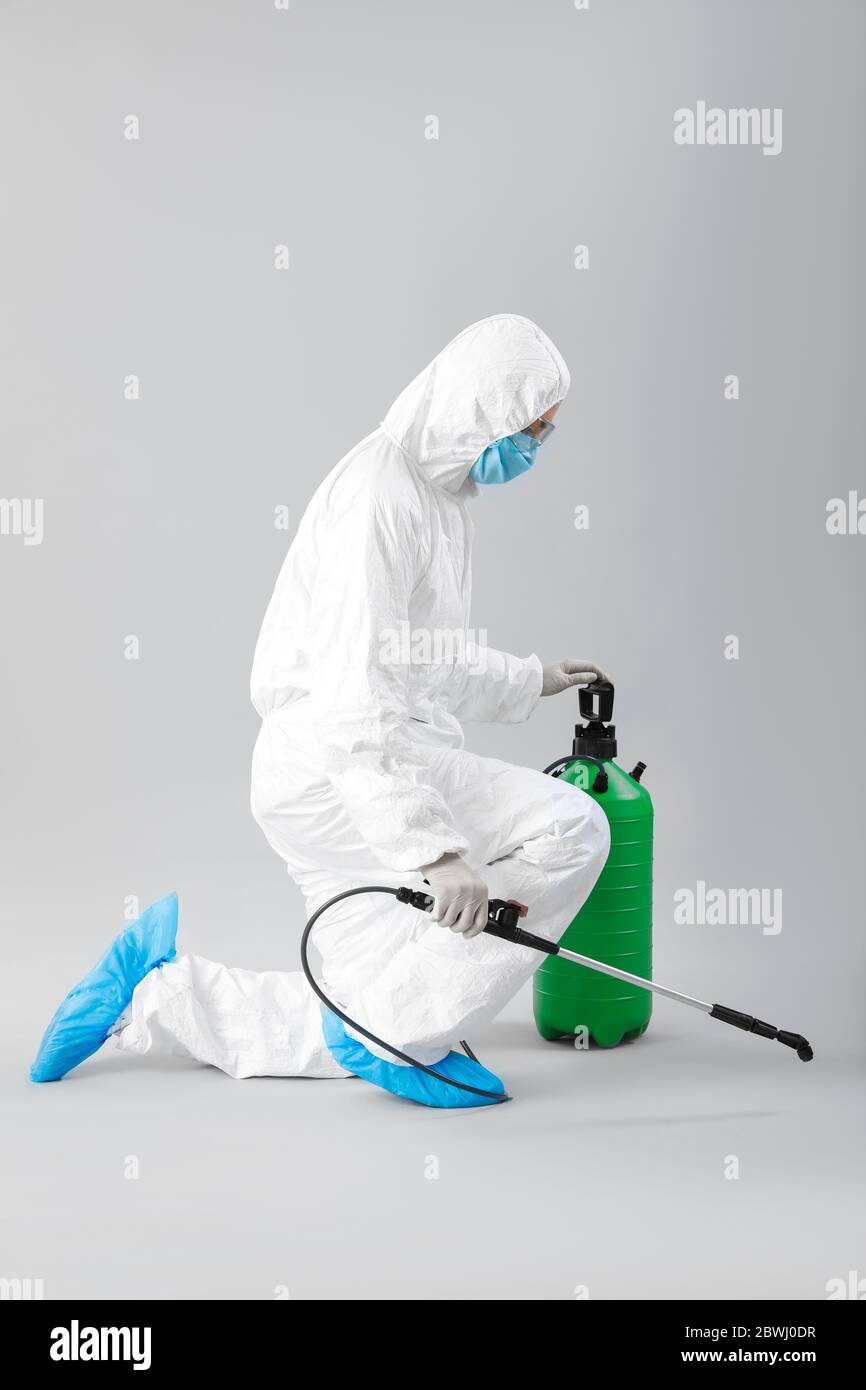 Worker in biohazard suit and with disinfectant on grey background Stock ...