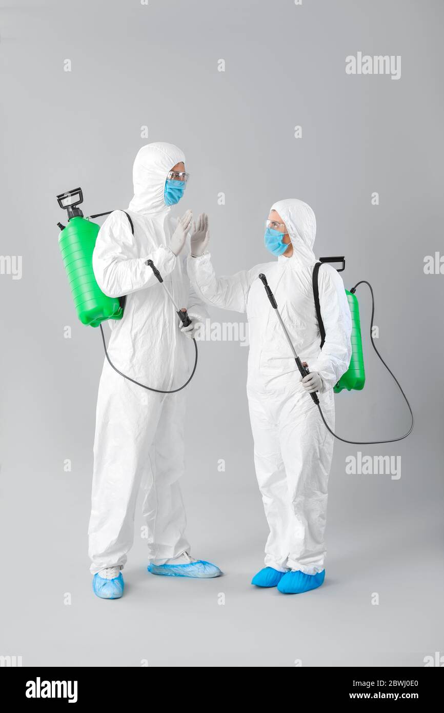 Workers in biohazard suits and with disinfectant on grey background ...