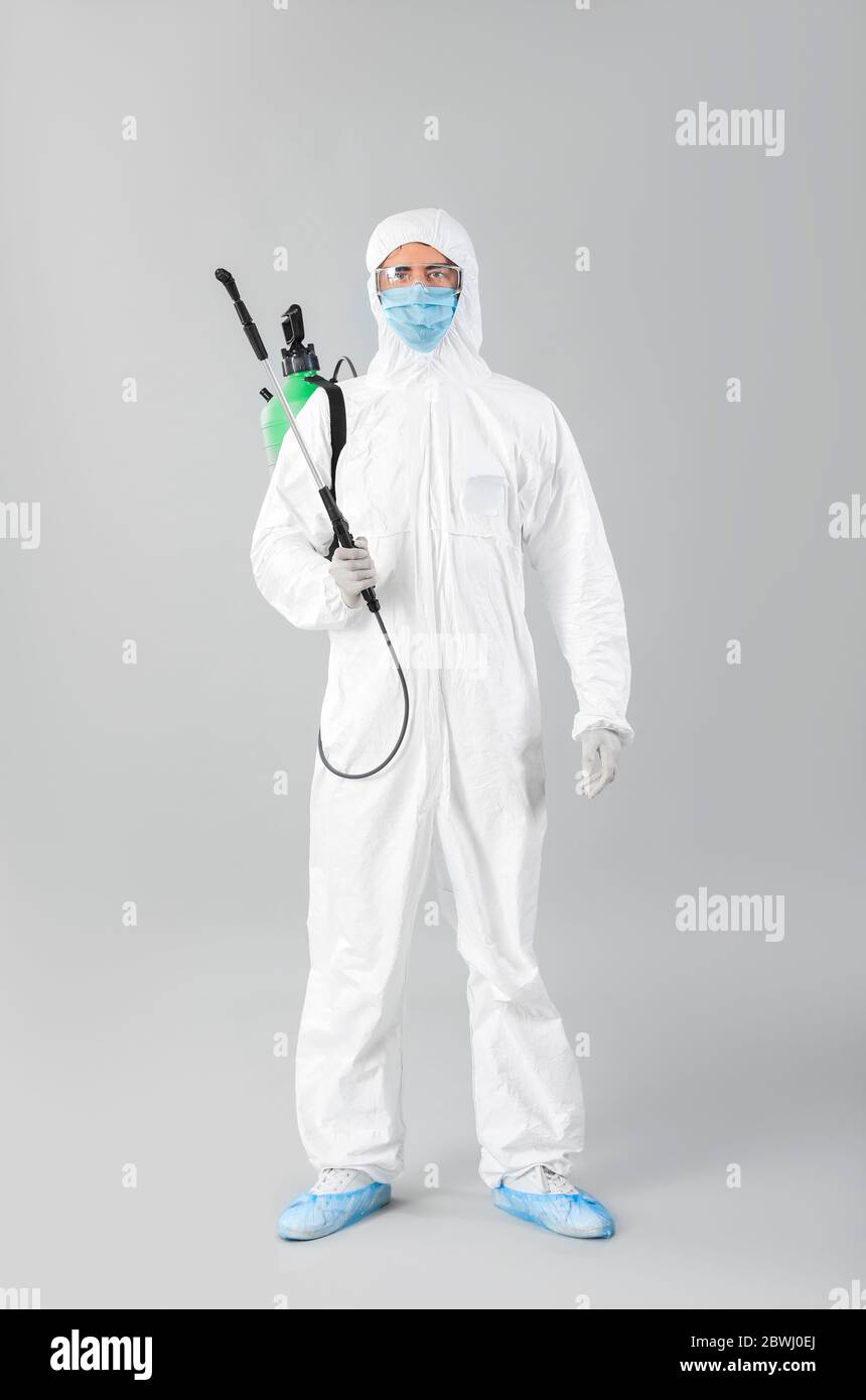 Worker in biohazard suit and with disinfectant on grey background Stock ...