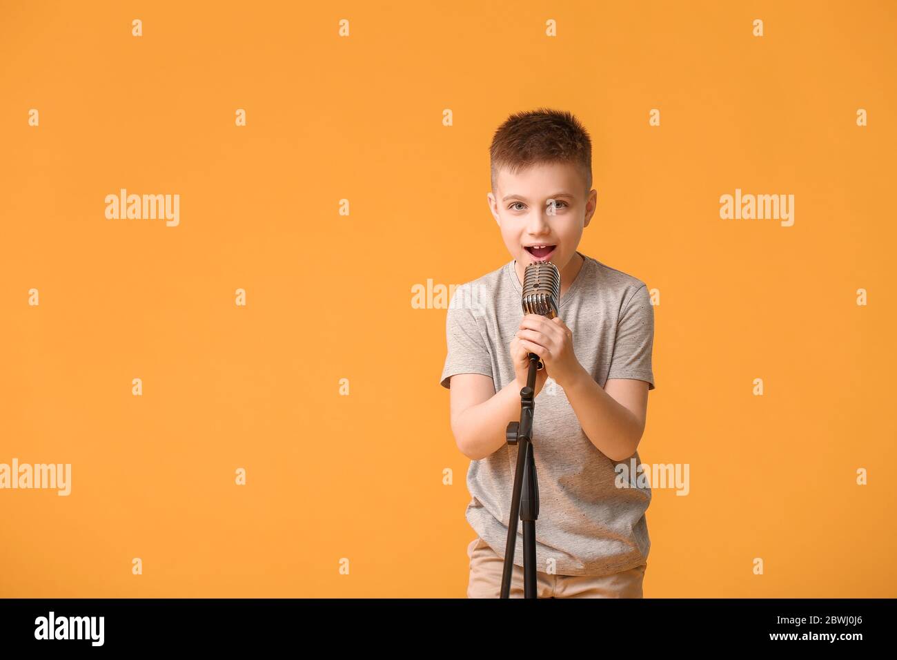 Cute little boy singing against color background Stock Photo - Alamy