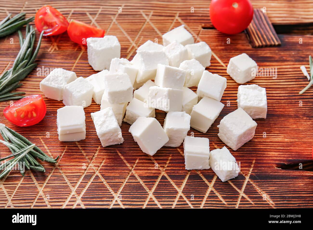 Tasty cut feta cheese with tomatoes and herbs on wooden board Stock ...