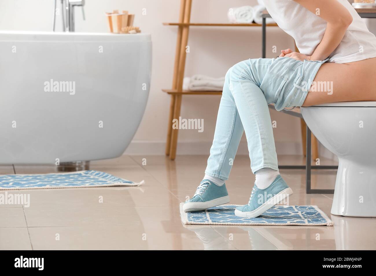 Young Woman With Hemorrhoids Sitting On Toilet Bowl In Bathroom Stock