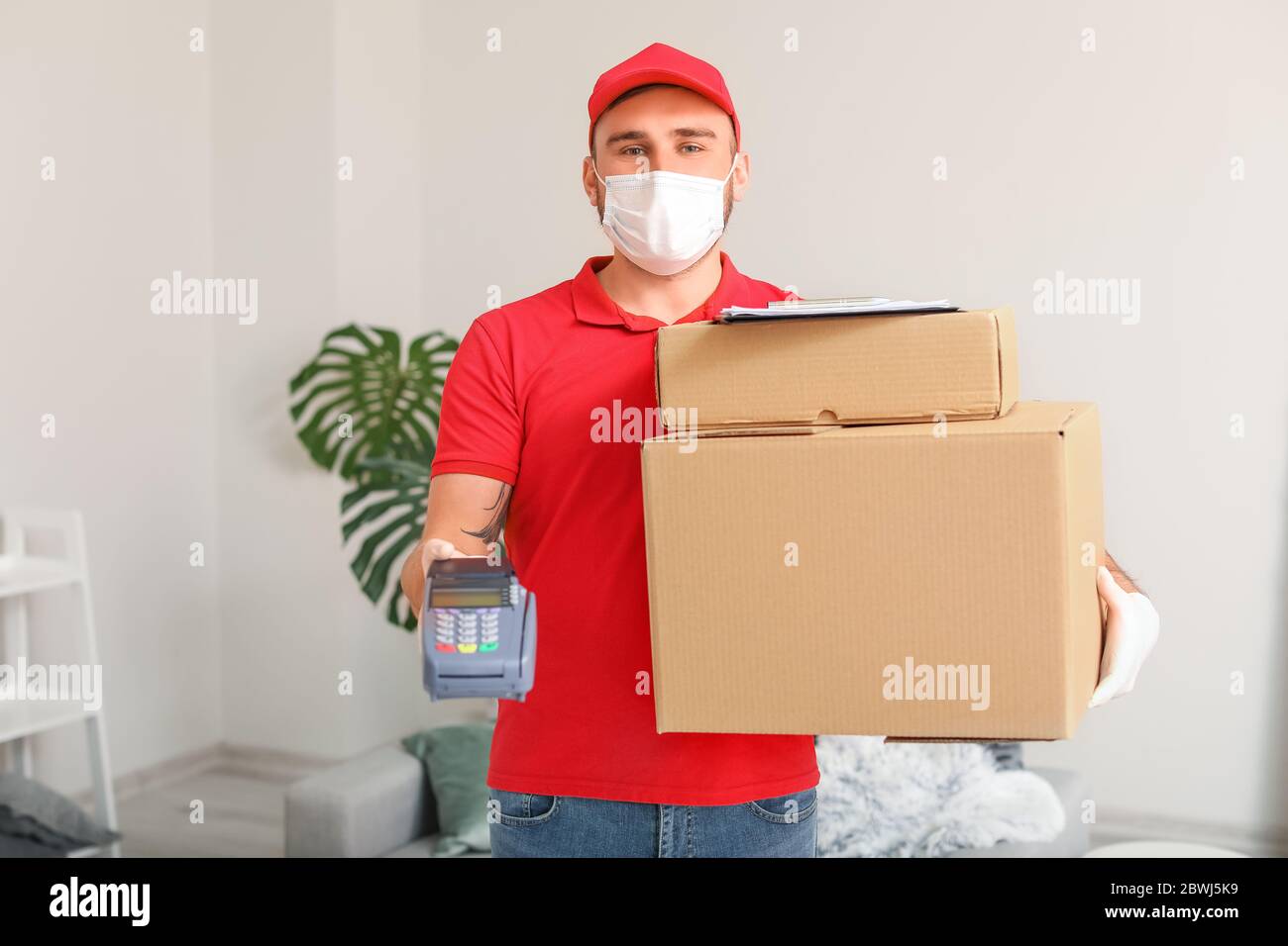 Male courier with boxes and payment terminal indoors Stock Photo - Alamy