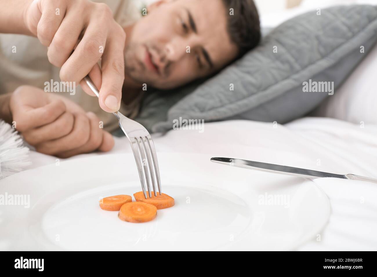 Sick man eating carrot while lying on bed. Concept of anorexia Stock ...