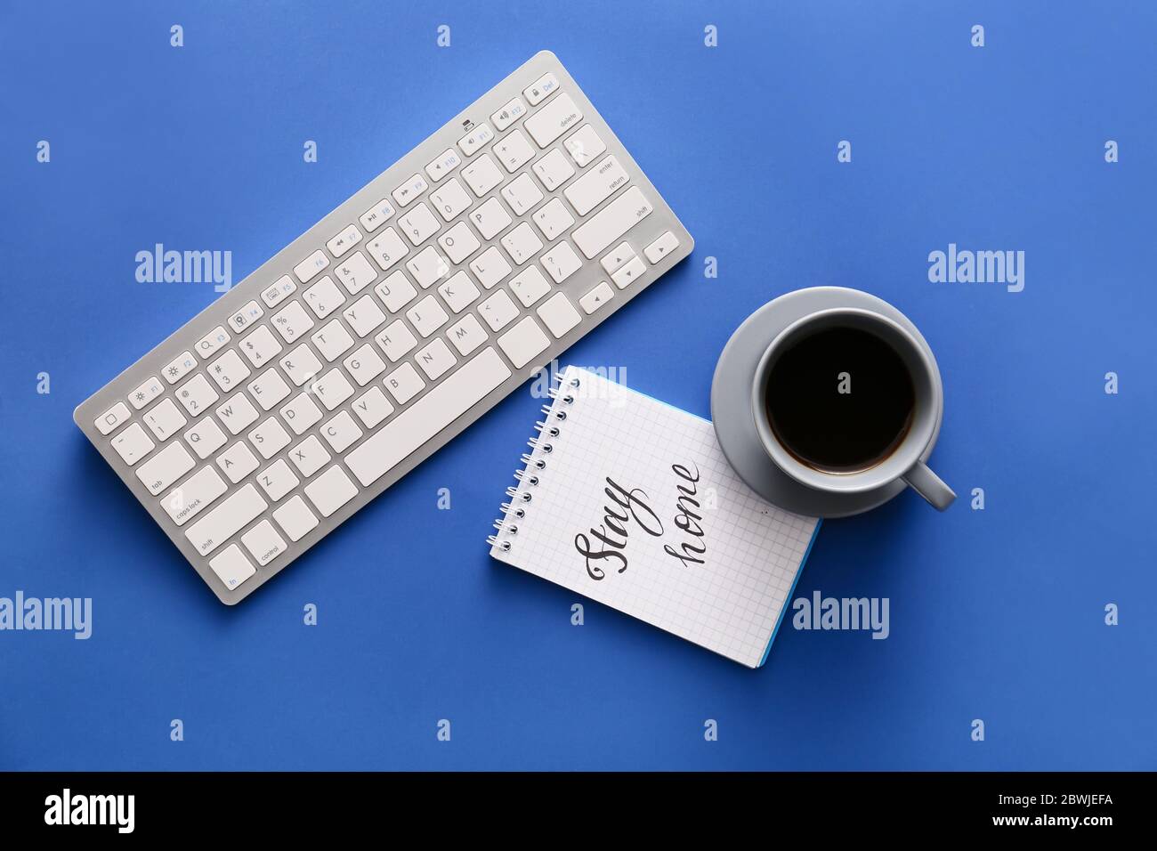 Computer keyboard with cup of coffee and notebook with text STAY HOME ...