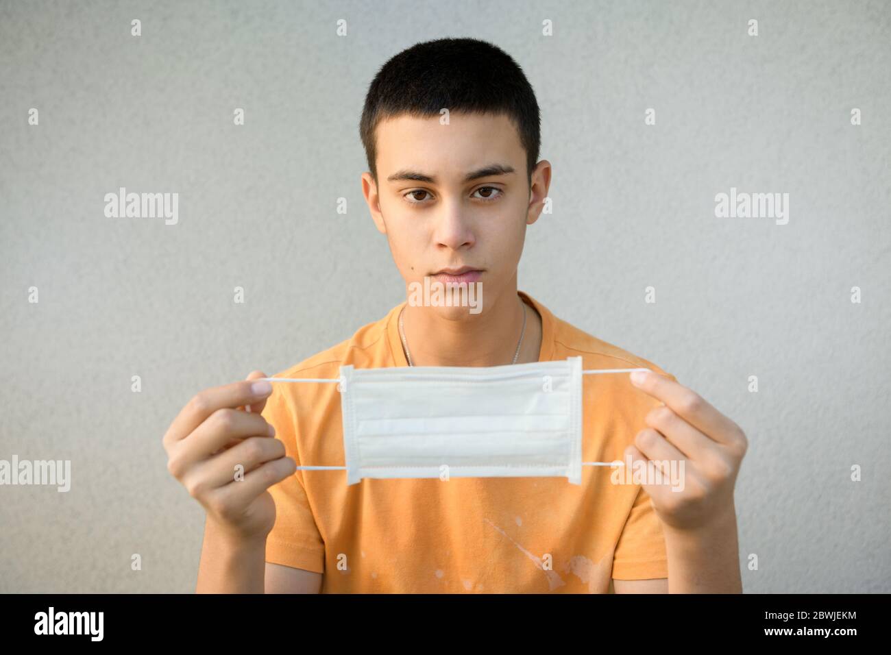 Young man holding up a disposable surgical face mask in front of his ...