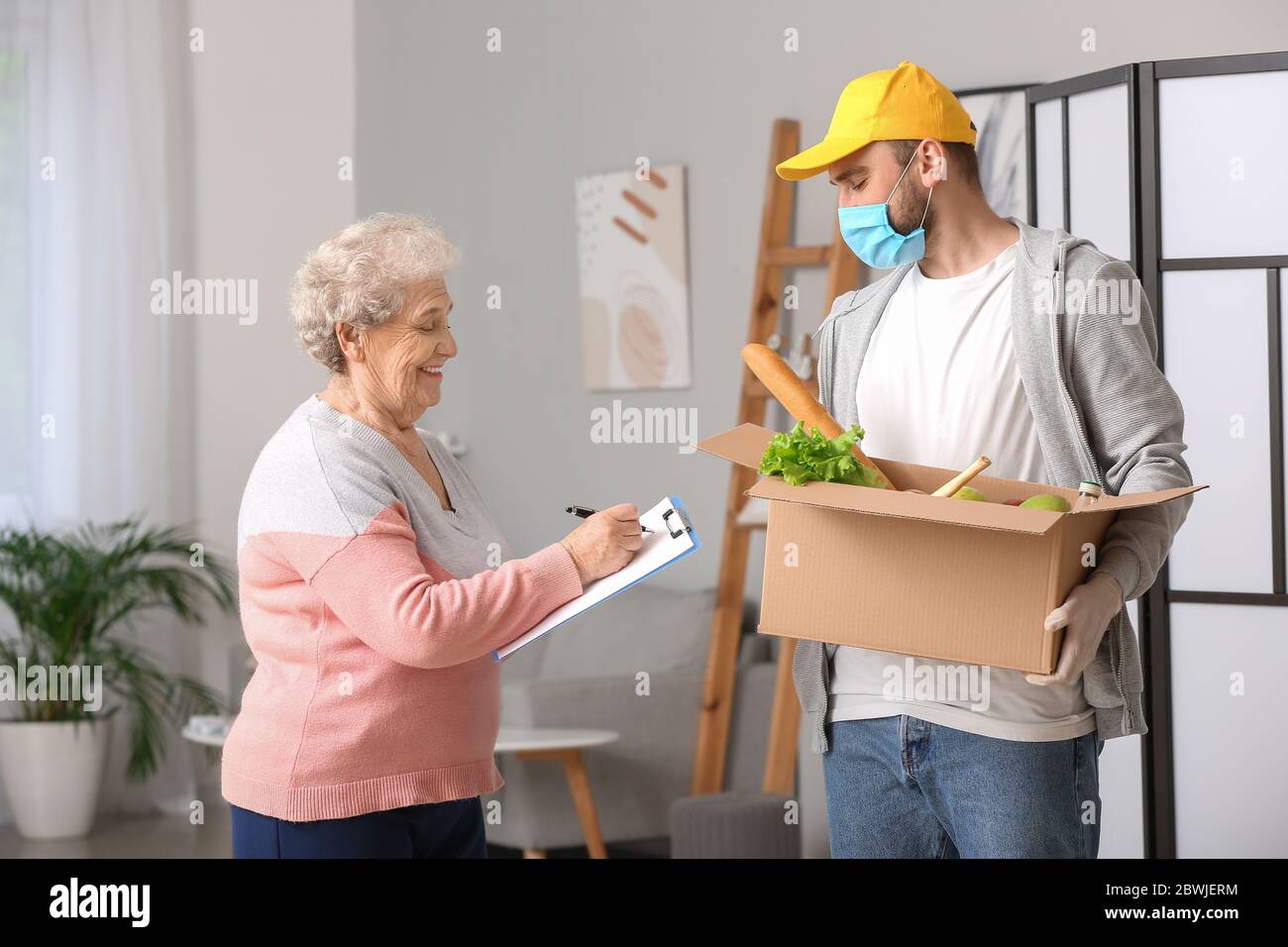 Senior woman receiving food from courier at home. Concept of epidemic ...