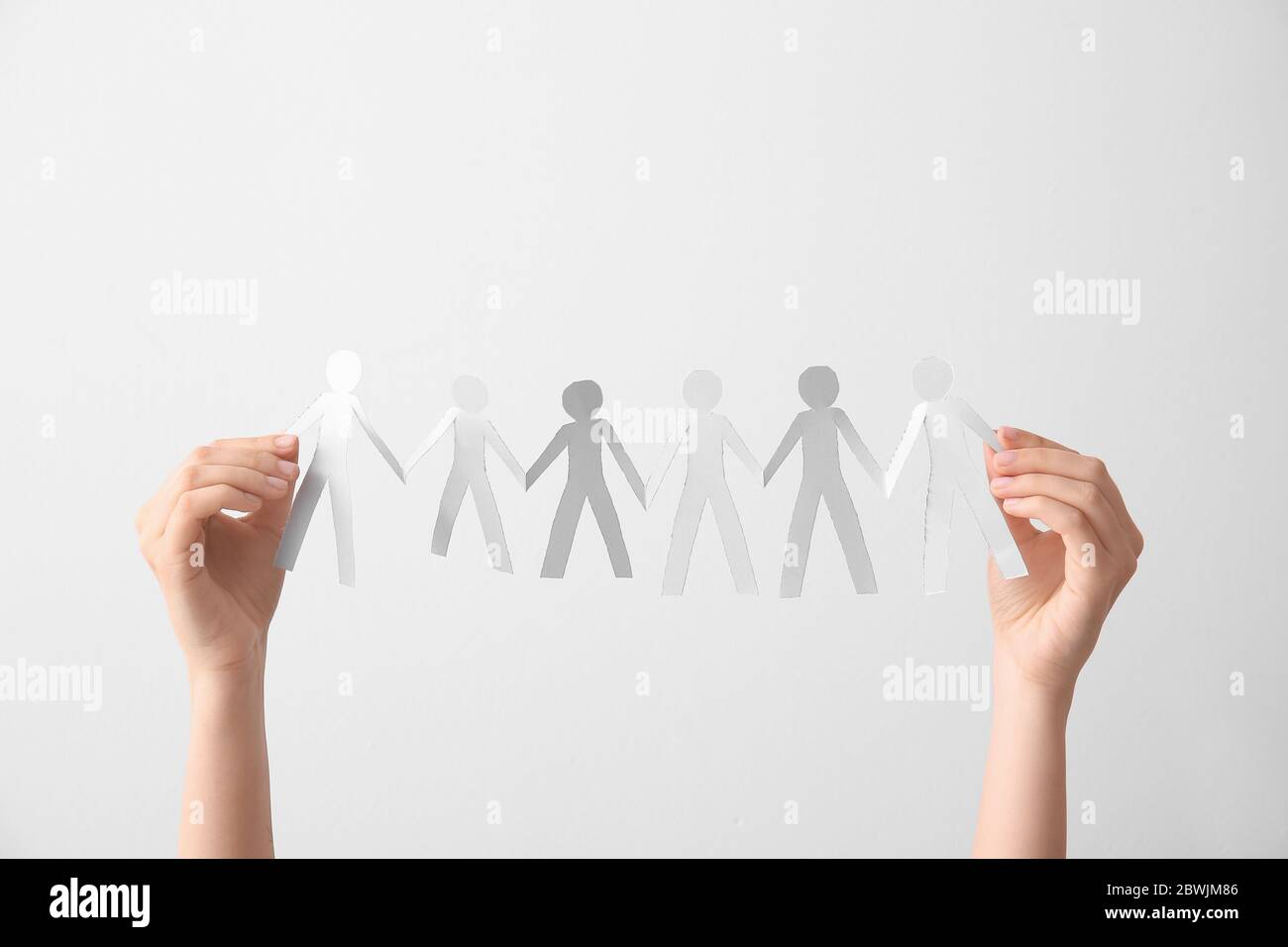 Female hands holding paper human figures on light background. Unity ...