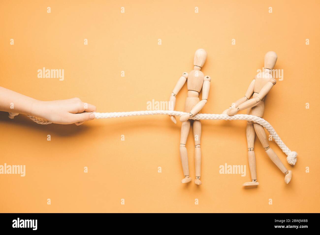 Female hand and wooden human figures pulling rope on color background ...