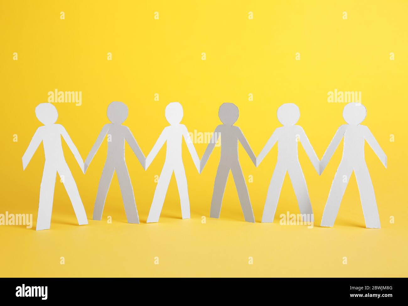 Paper human figures holding hands on color background. Unity concept ...