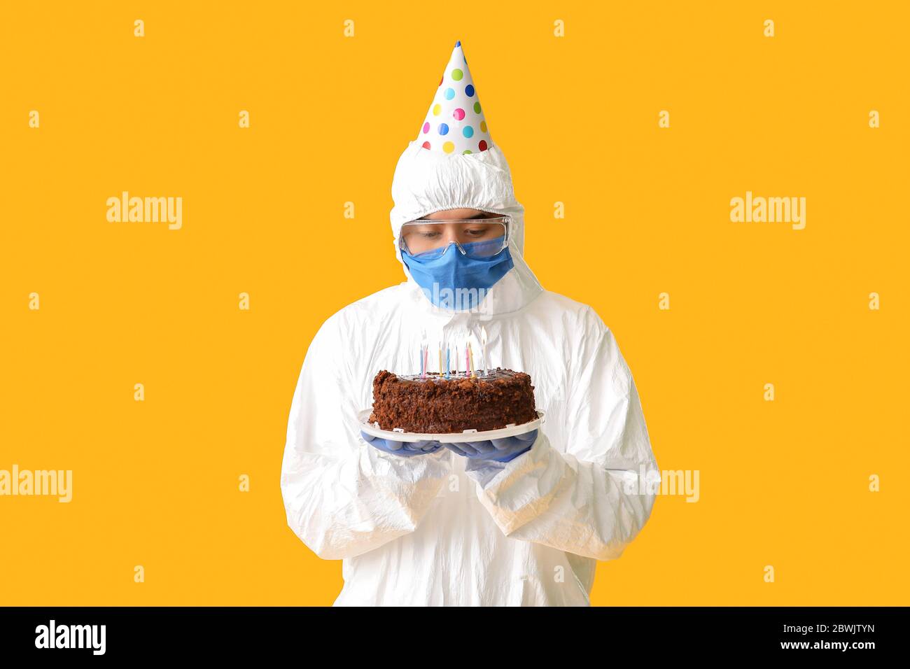Asian man in biohazard suit and with Birthday cake on color background ...