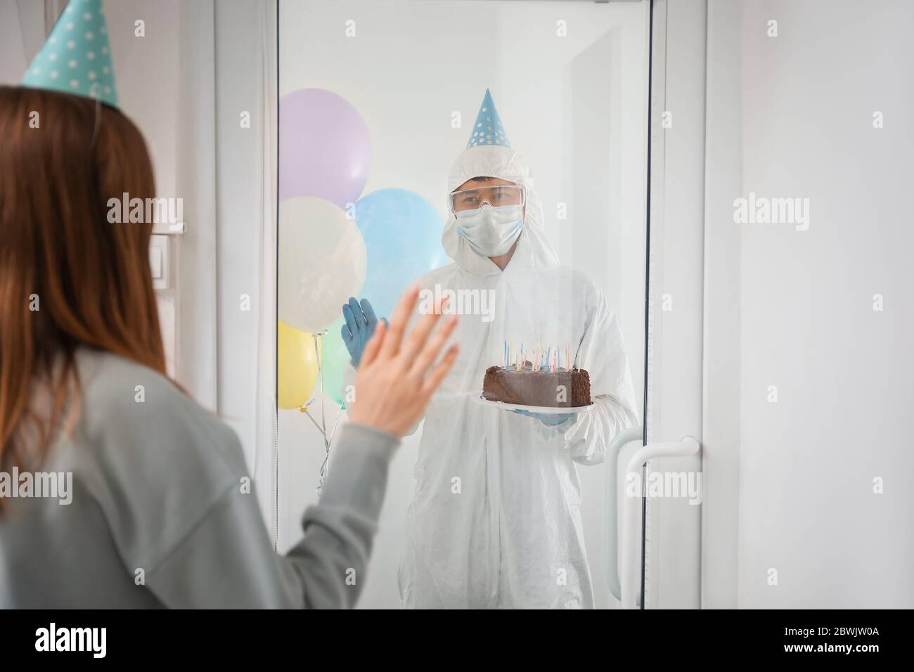 Asian man in biohazard suit and with Birthday cake visiting his friend ...