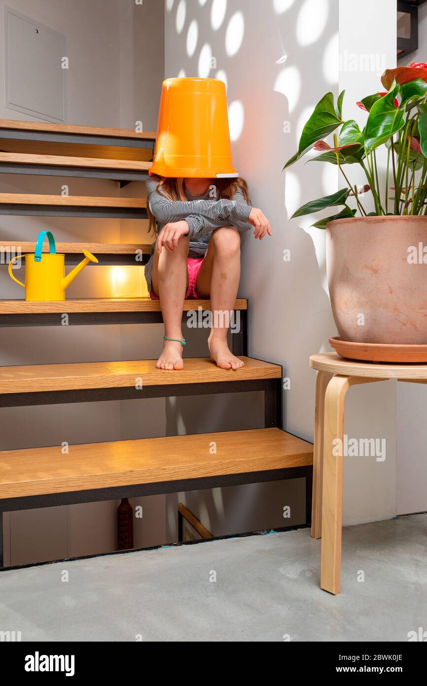 Little girl with bucket on her head takes care of the flowers of her ...