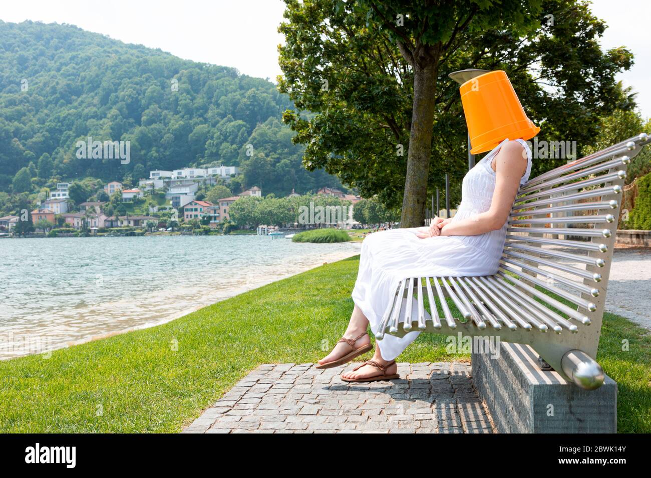 Young woman sitting on a bench by the lake with an orange bucket on her ...