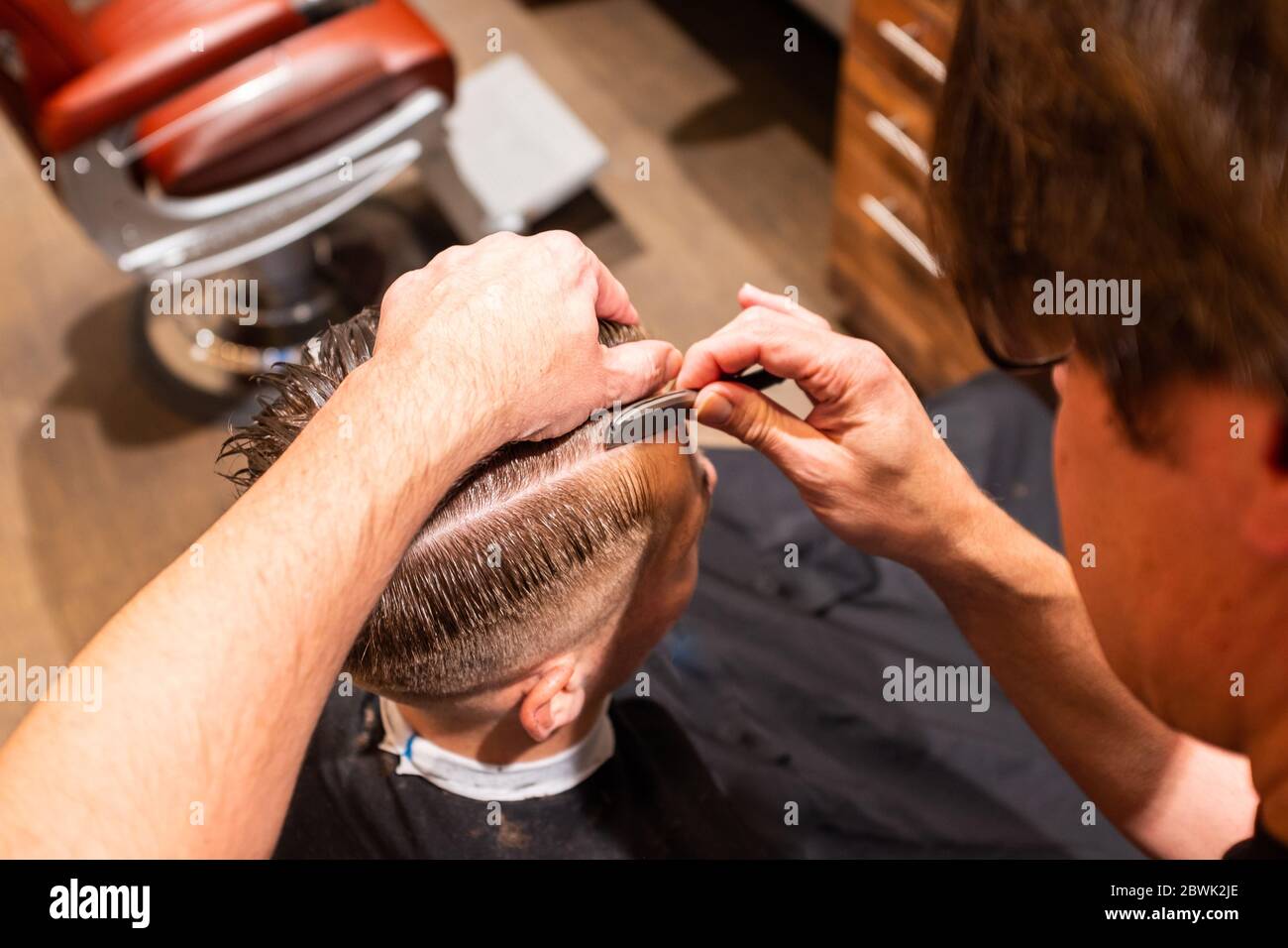 Barber shaves the parting of a young man's hair with a razor blade in ...