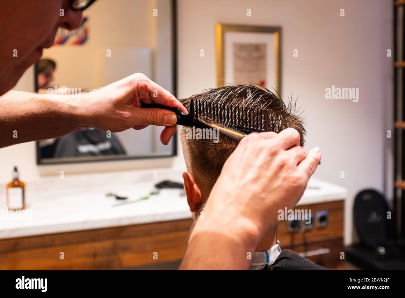 Barber cuts the hair of a young man with scissors and a comb in his ...