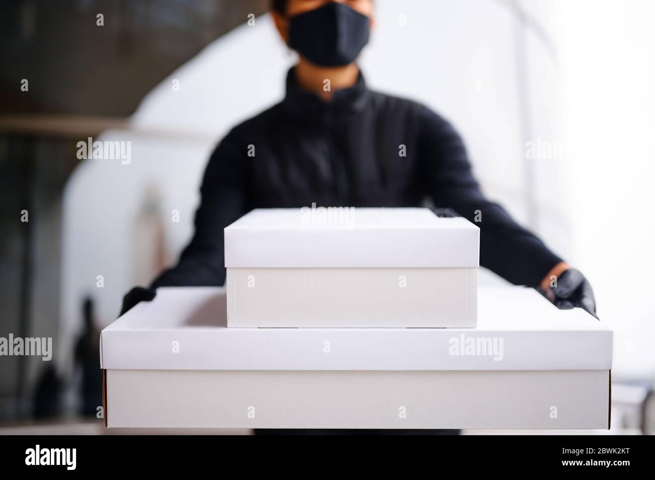 Young delivery worker in black face mask and black gloves holding white ...