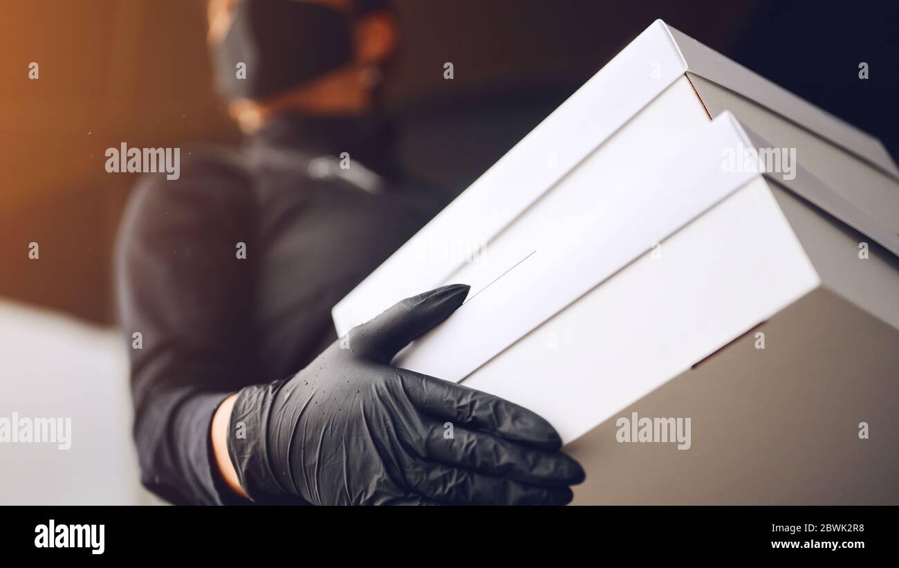 Young delivery man in face mask and gloves holding white cardboard box ...