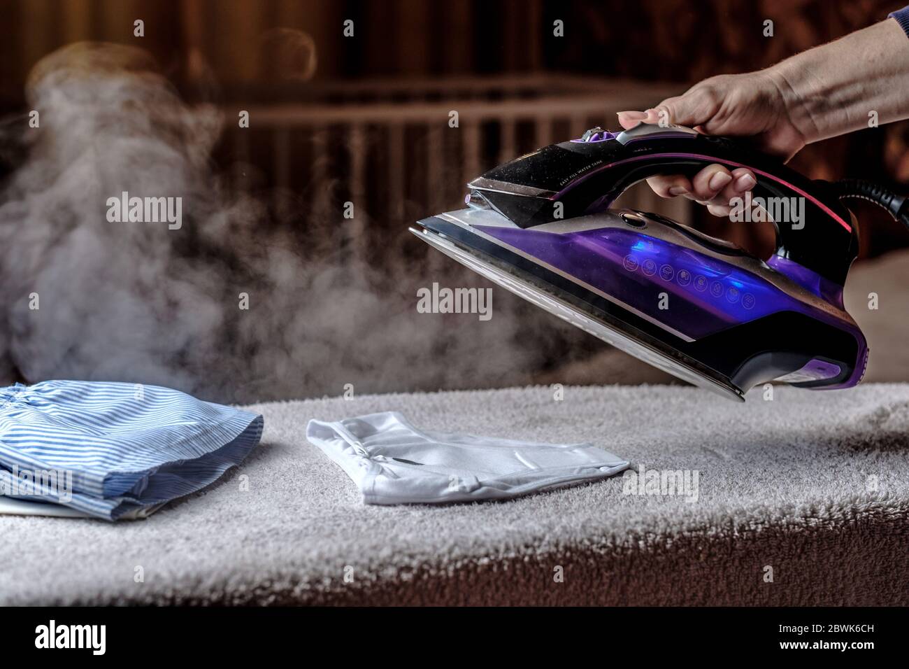 Closeup female hand ironing clothes on the table. Puffs of hot steam ...