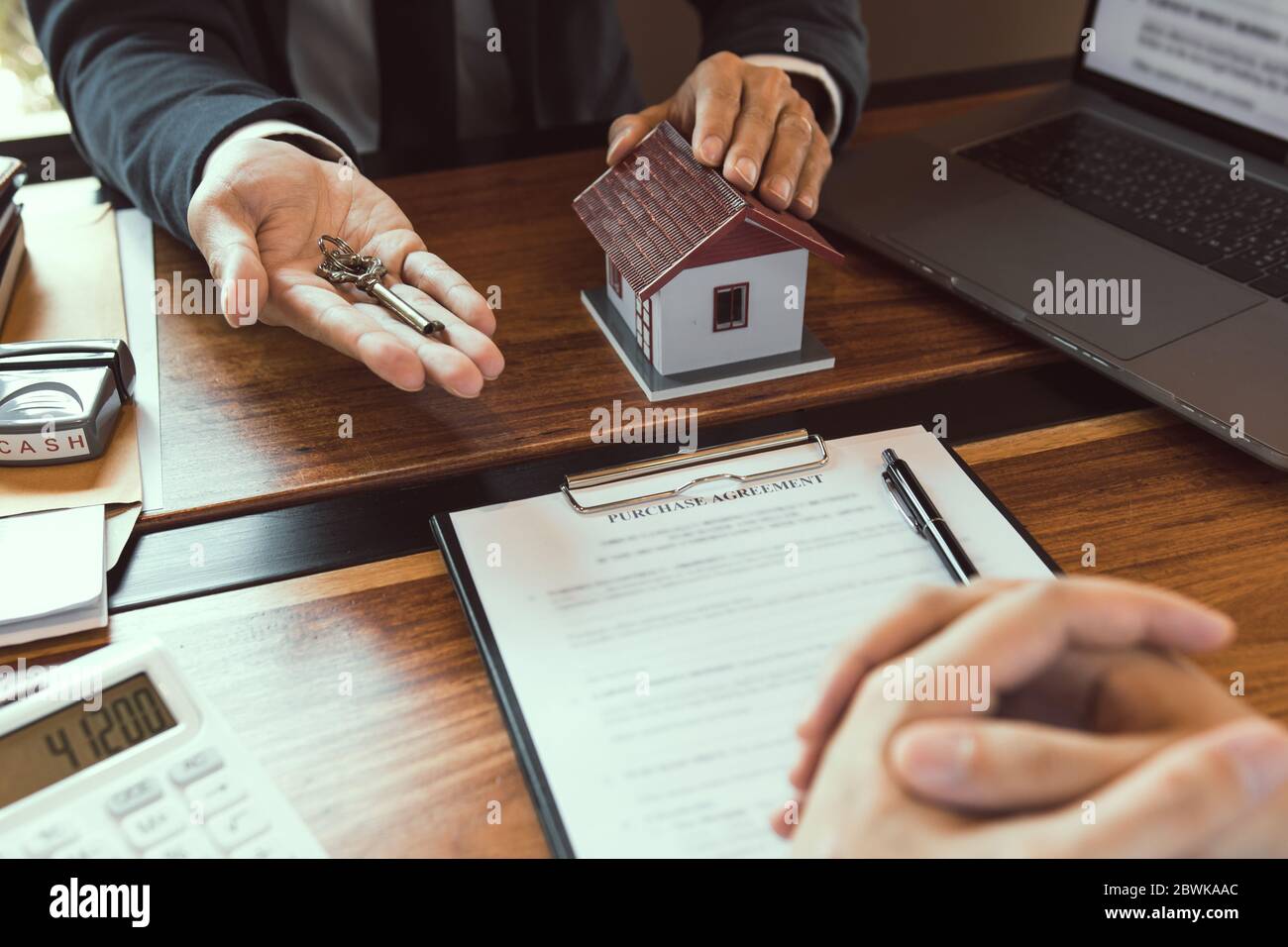 Hand of real estate agent passes the key to new homeowners in office ...