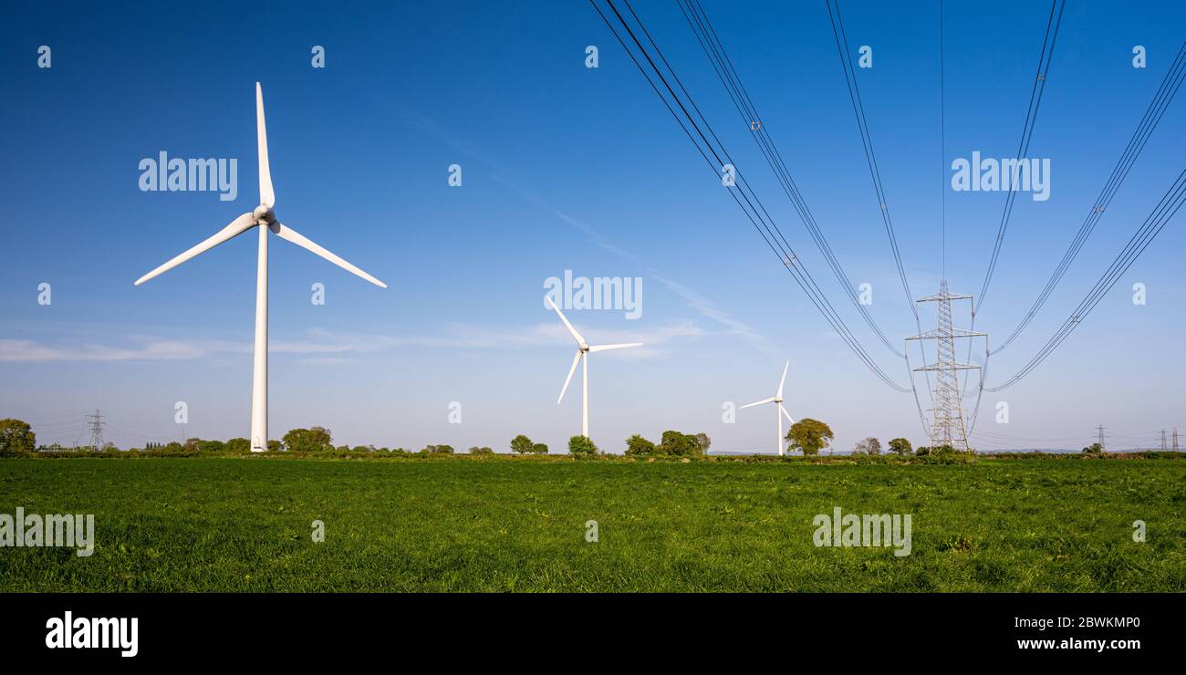Wind turbines stand in farmland fields beside National Grid high ...