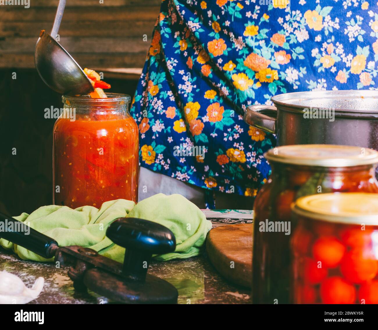 a man in a colored apron clogs tomatoes and Lecho sauce in glass jars ...