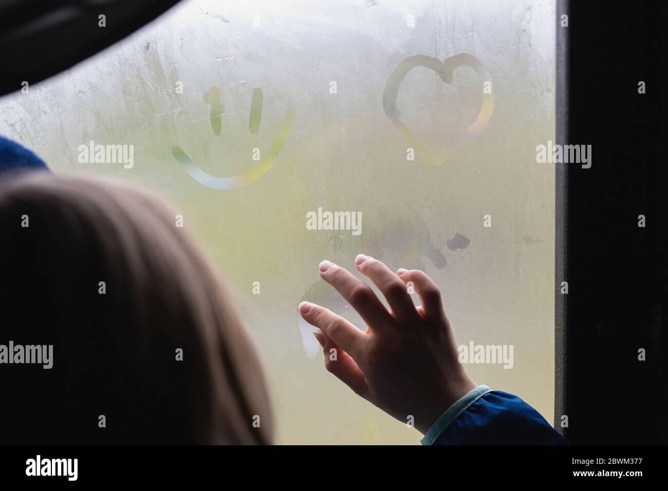 girl or young women hand draws on misted, foggy window. finger on wet ...