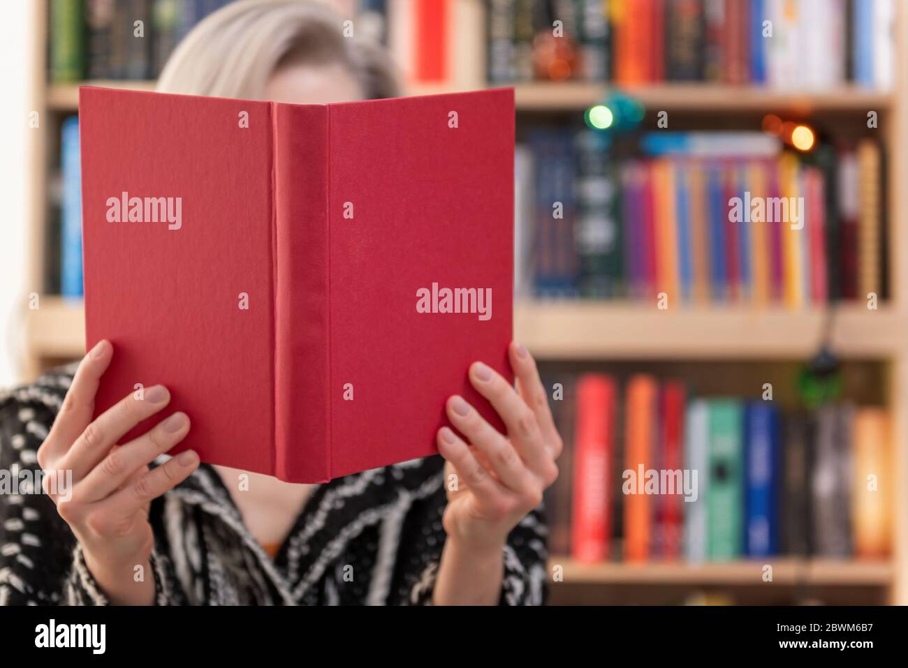 Woman sitting on a floor and holding book in front of face on blurred ...