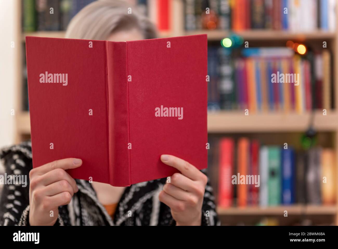 Woman sitting on a floor and holding book in front of face on blurred ...