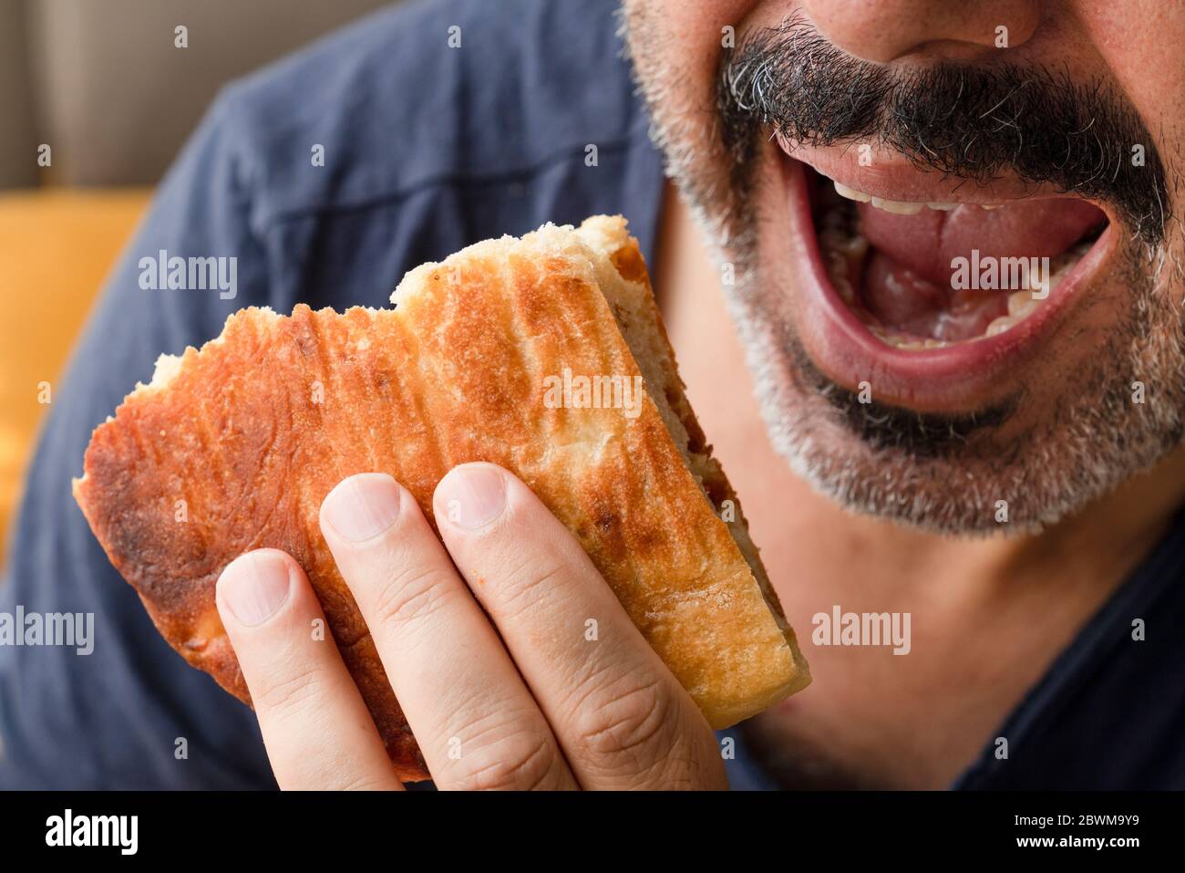 Mustachioed man holds bread and is ready to bite bread. Man opens mouth ...