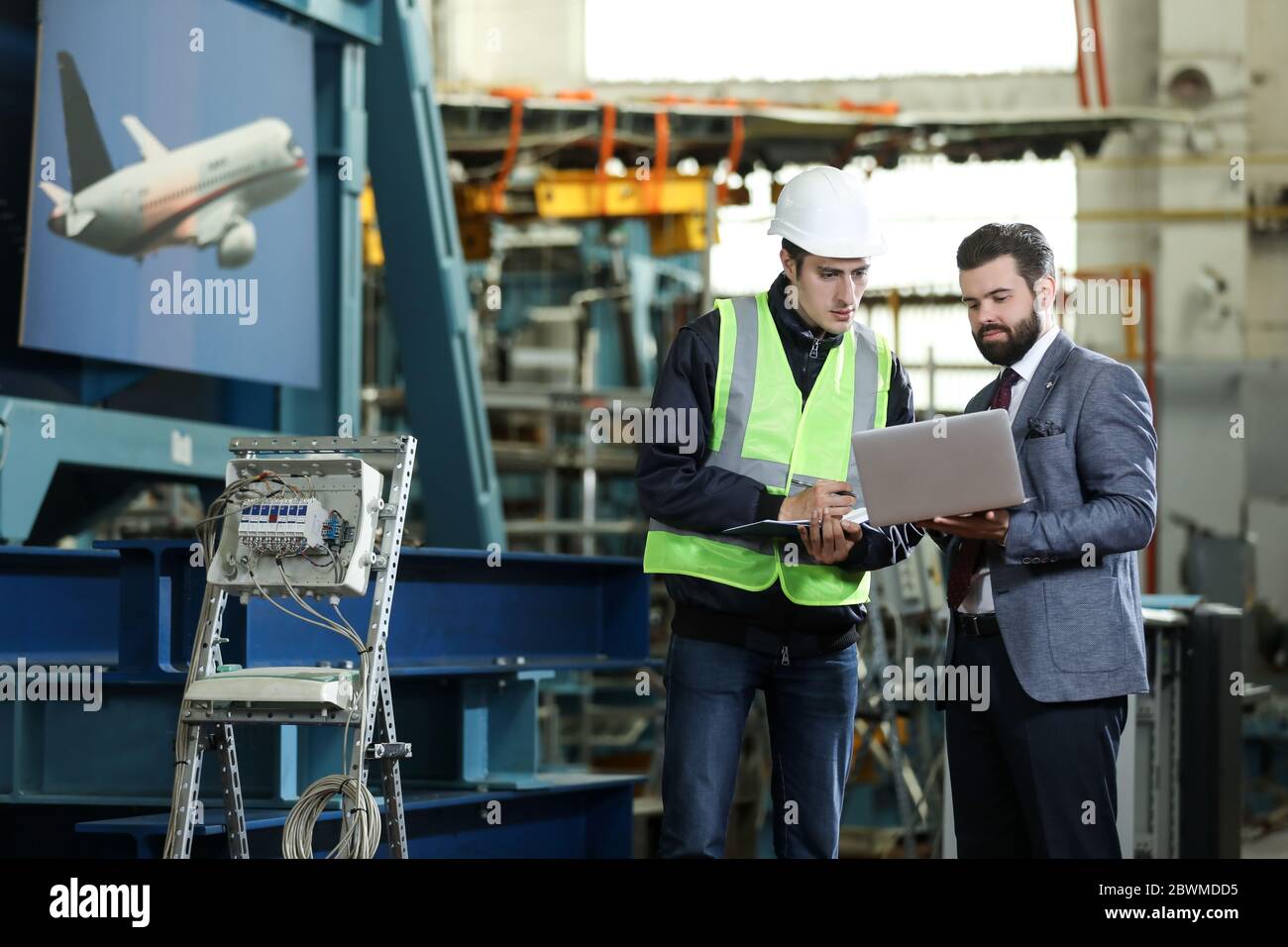 Portrait of a solid businessman with laptop and factory engineer in a ...