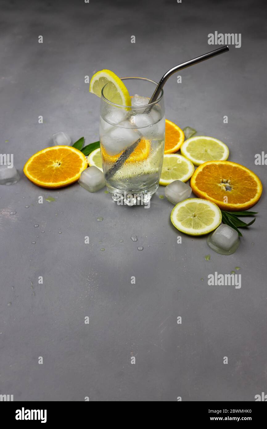 Glass full of cold refreshing sparkling water and citrus fruits in the back with melting ice ...