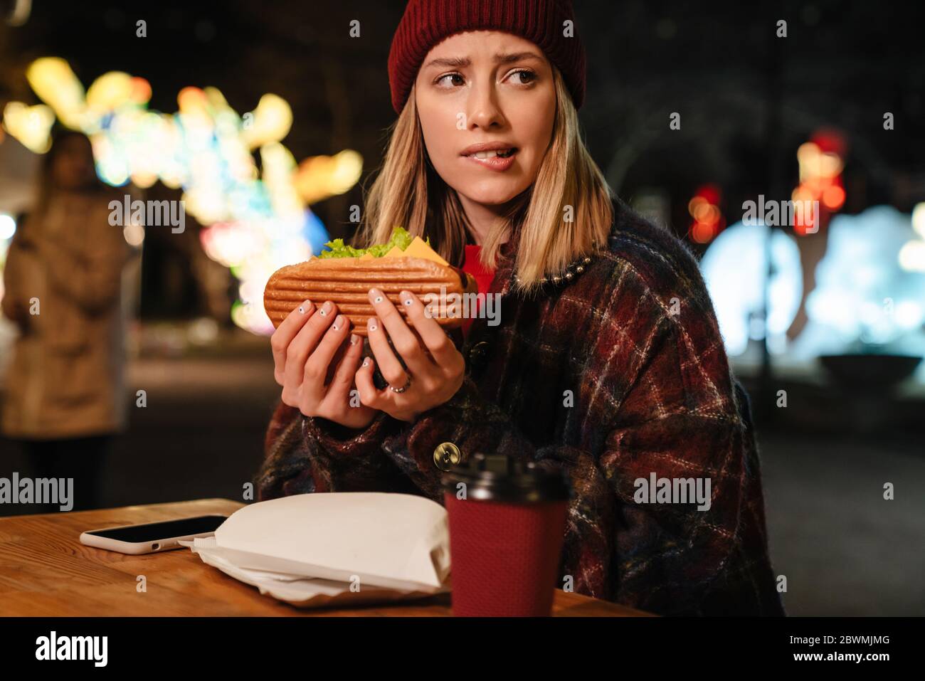 Photo of scared nice woman eating sandwich while sitting in street cafe ...