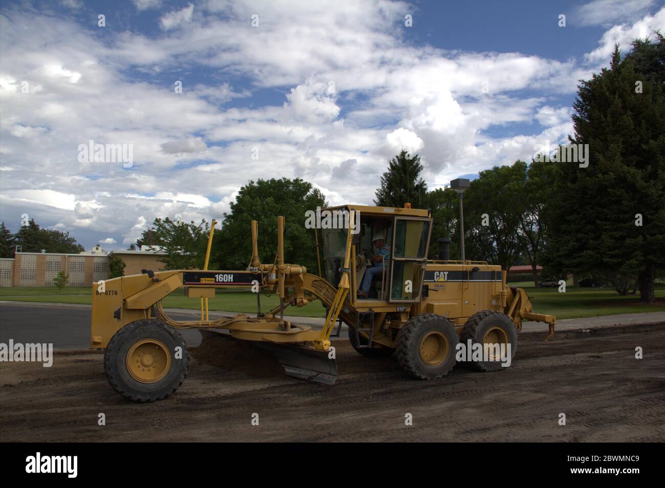 Construction worker on motor grader, bladeing street before paving ...