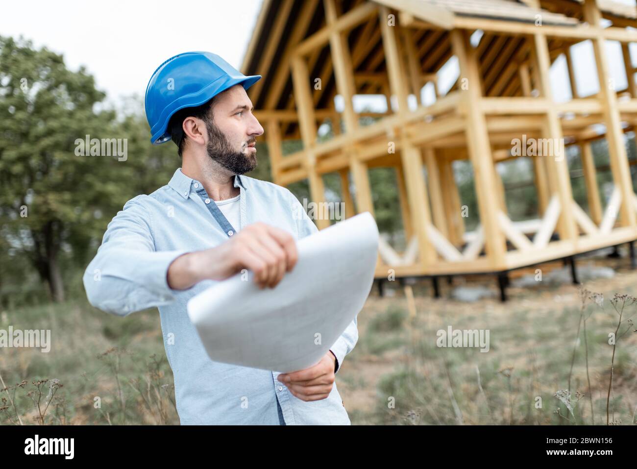 Architect or builder standing with blueprints near the wooden house ...