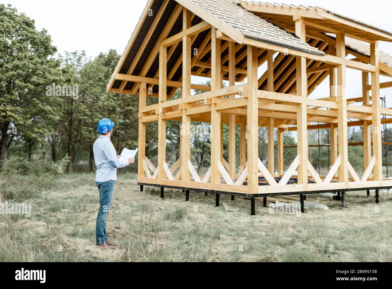 Architect or builder standing with blueprints near the wooden house ...