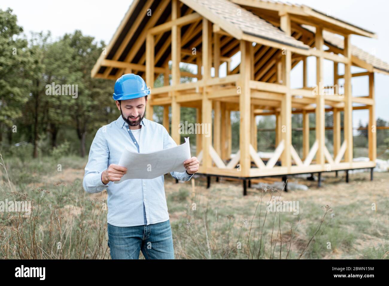 Architect or builder standing with blueprints near the wooden house ...