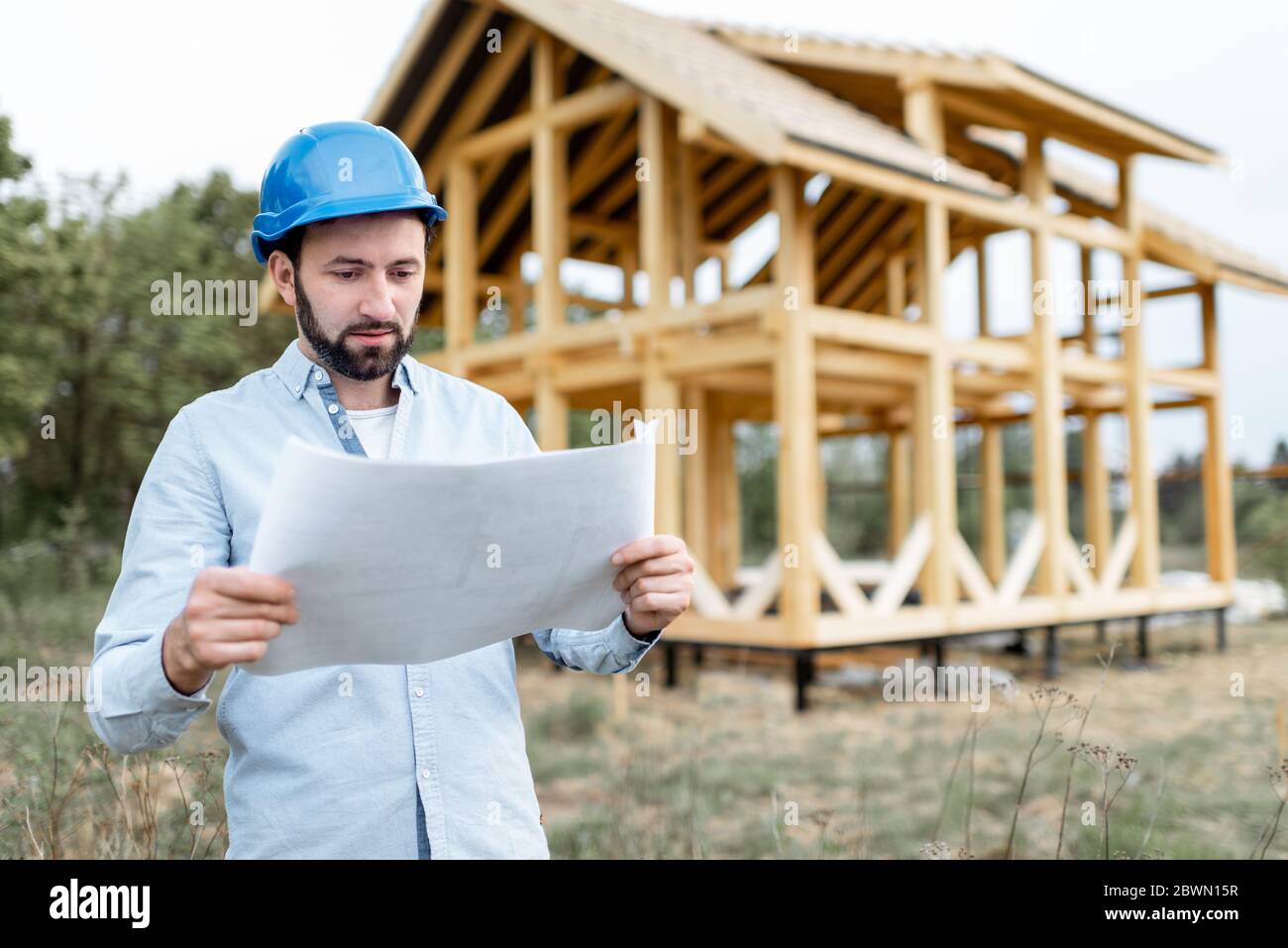 Architect or builder standing with blueprints near the wooden house ...