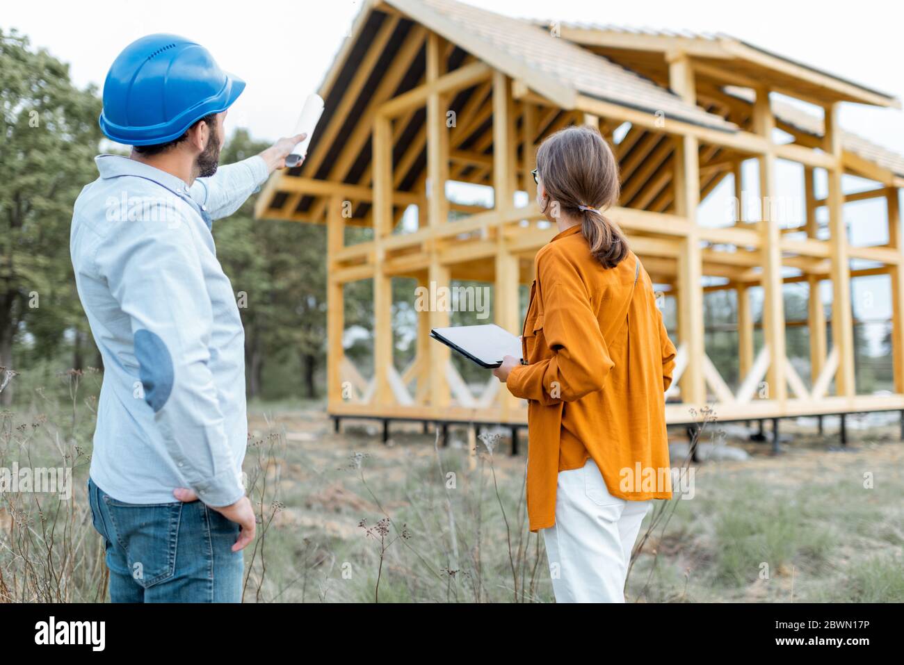 Builder with a female client near the wooden house structure on the ...