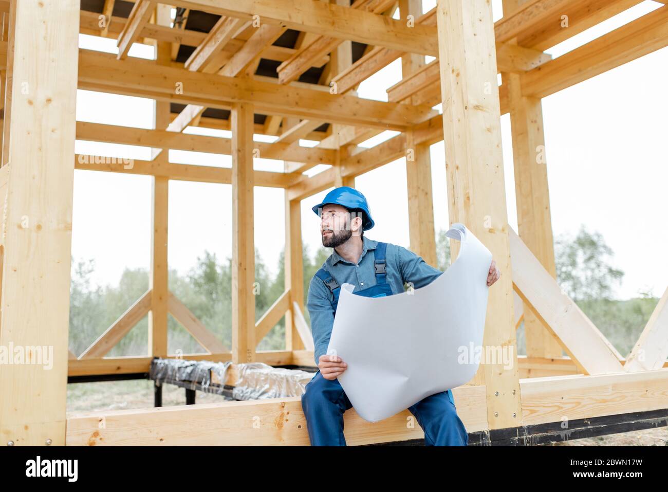 Builder in blue overalls and hard hat with blueprints on the ...