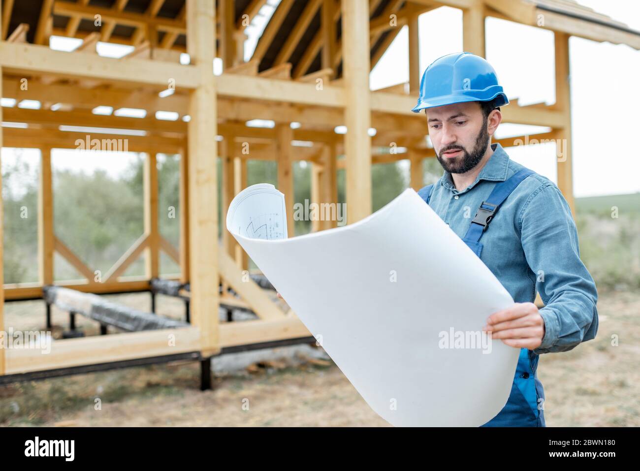 Builder in blue overalls and hard hat with blueprints on the ...