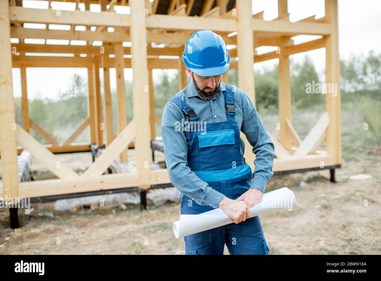 Builder in blue overalls and hard hat with blueprints on the ...