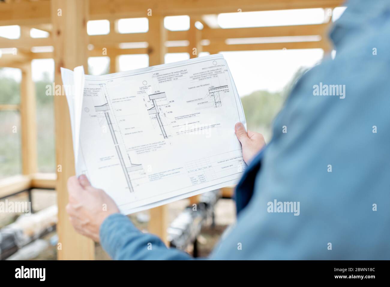 Builder with blueprints on the construction site, building wooden frame ...