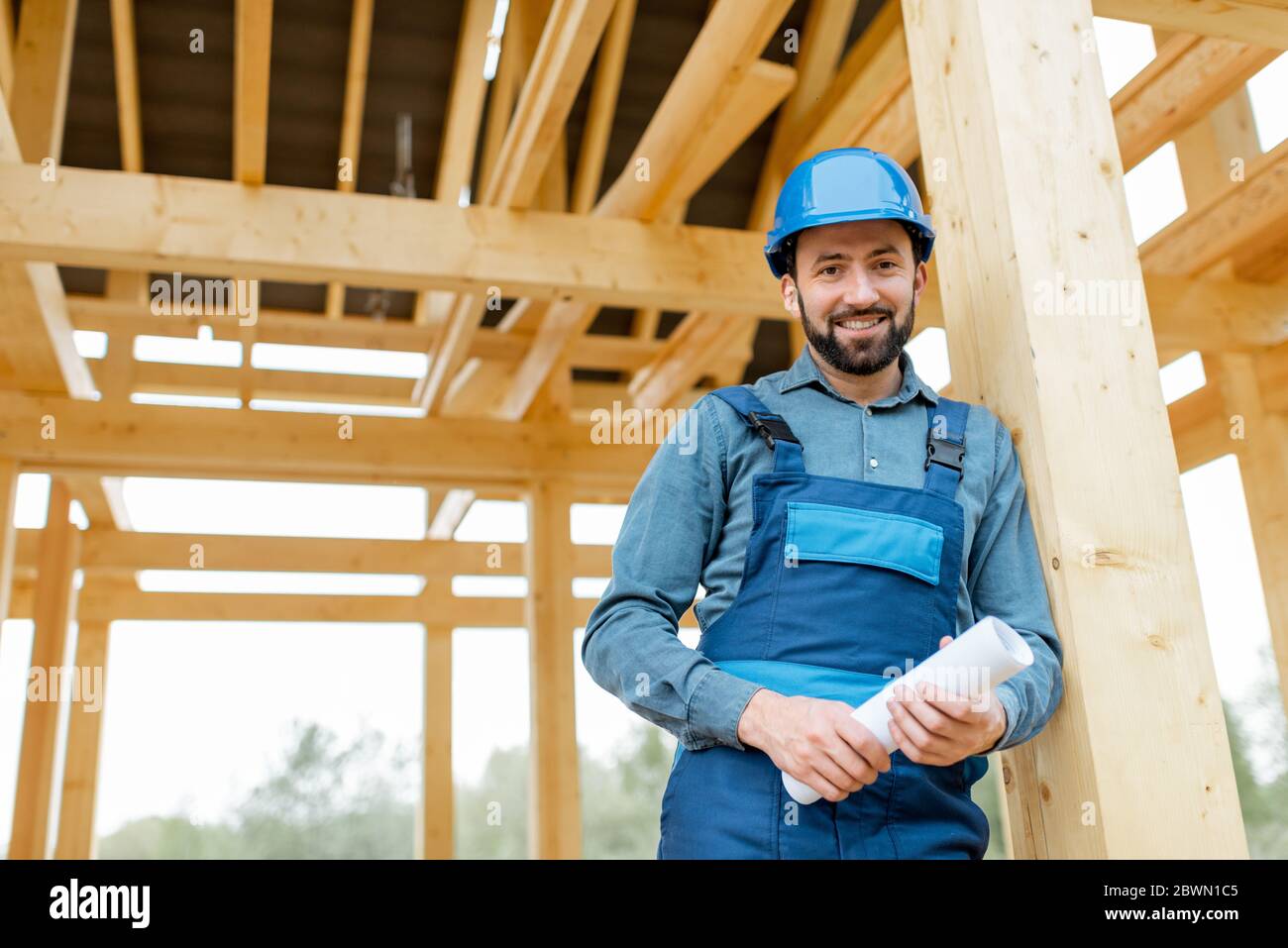 Portrait of a handsome builder in blue overalls and hard hat with ...