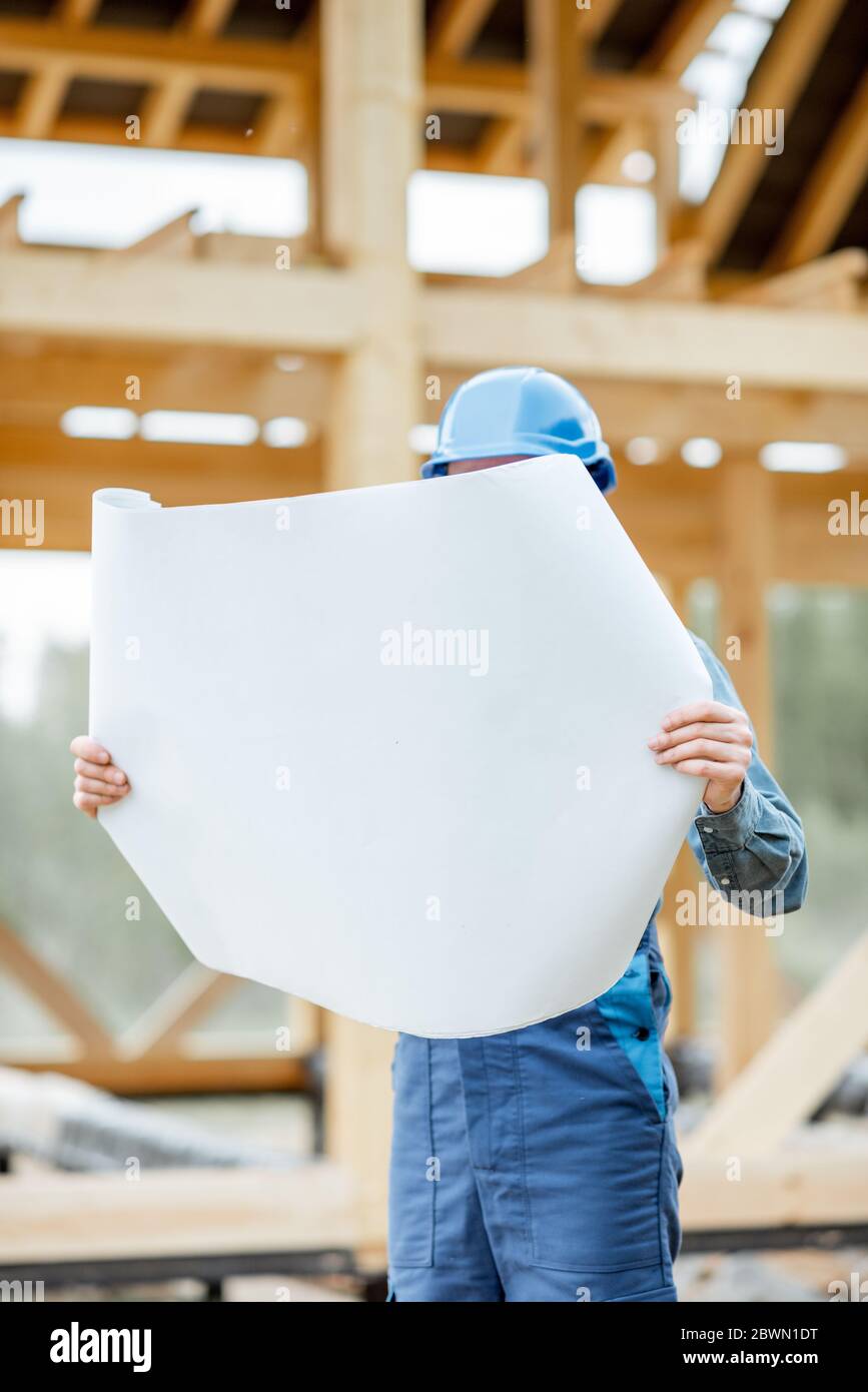 Builder in blue overalls and hard hat looking on the blueprints on the ...