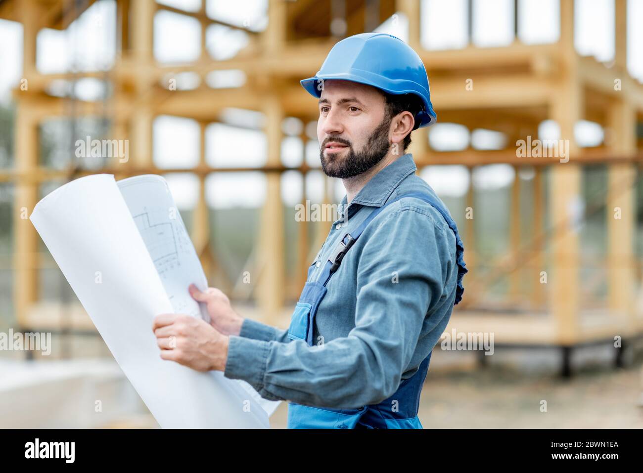 Portrait of a confident builder in blue overalls and hard hat standing ...