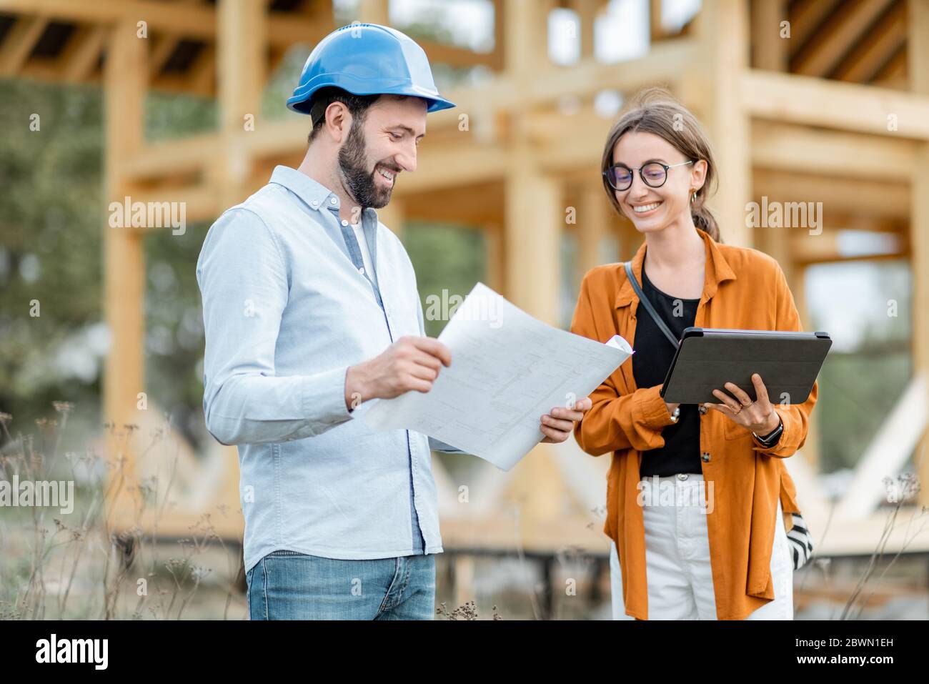 Builder with a female client near the wooden house structure on the ...