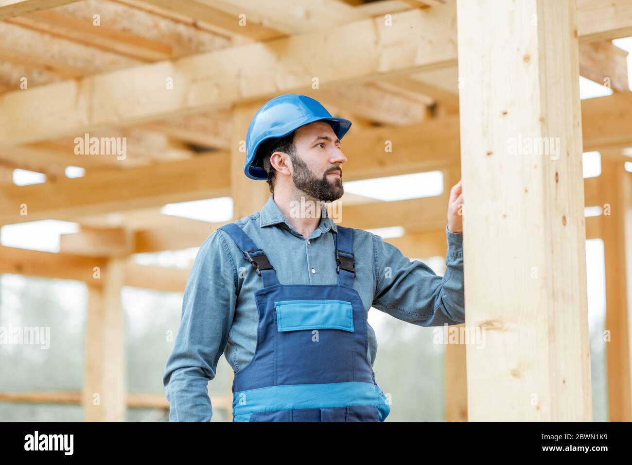 Portrait of a handsome and cofident builder in blue overalls and hard ...