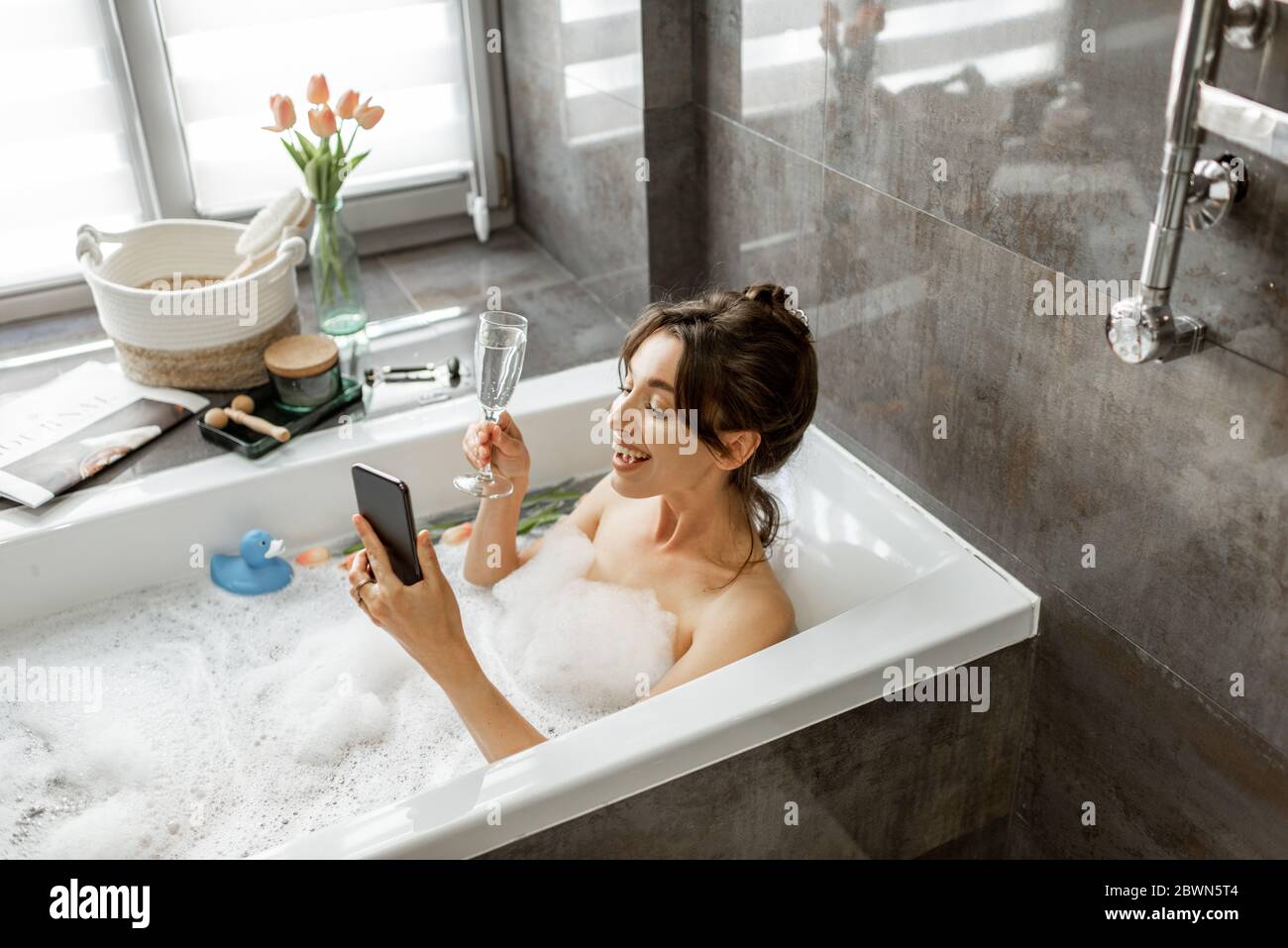 Young Woman Taking A Bath Drinking Sparkling Wine Talking On Phone
