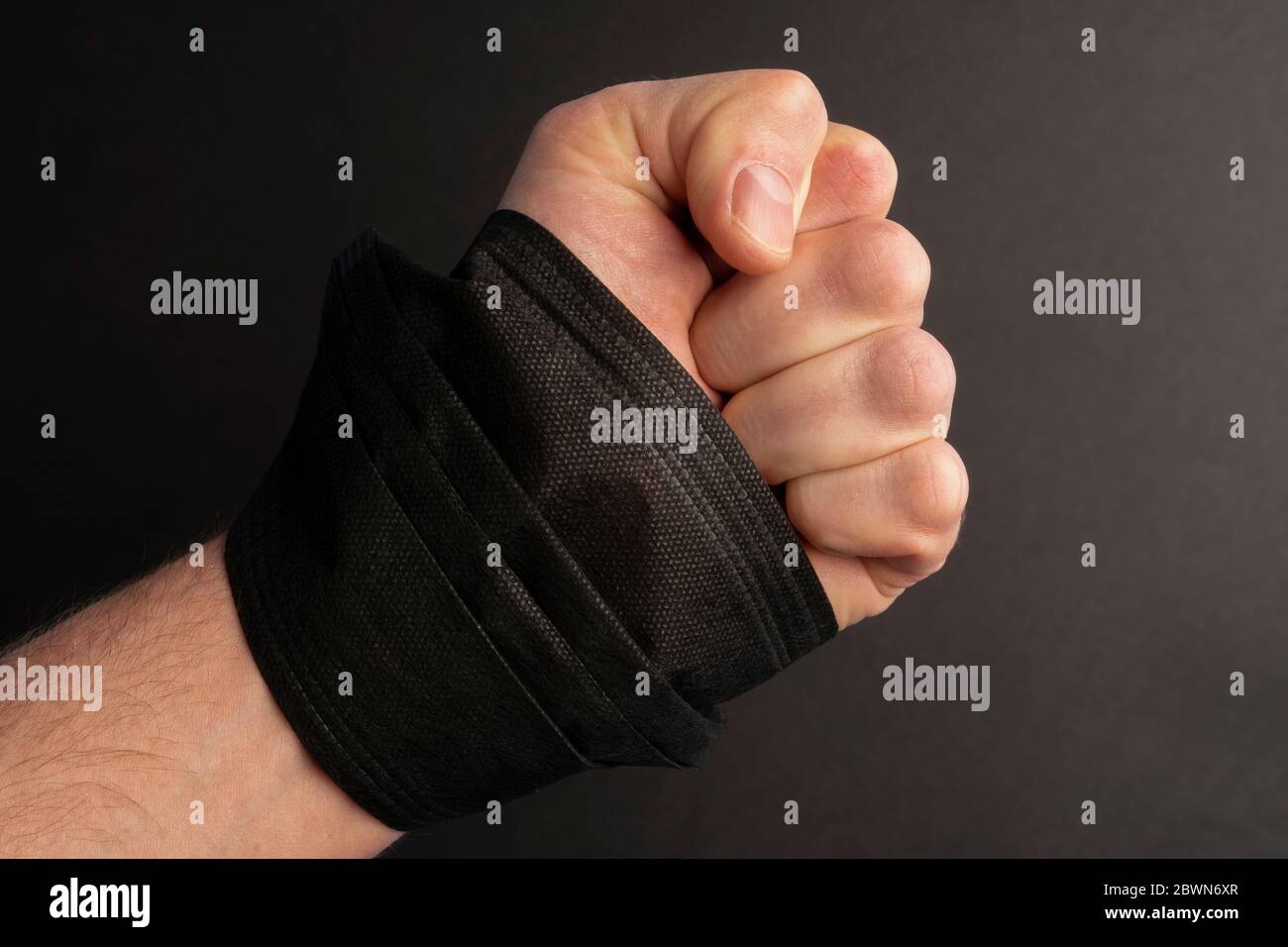 Fist with a black mask in his hand on a black background. A symbol of ...